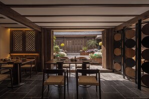 Uma sala de jantar em estilo japonês tradicional, com tatames, mobiliário de madeira e vista para um jardim com portão de madeira.