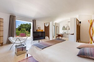 Quarto moderno com uma cama grande, televisão, área de estar e vista para o verde lá fora.