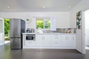 Cozinha moderna com armários brancos, geladeira de aço inoxidável, micro-ondas e janela com vista para o verde.