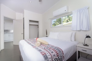 Quarto de hotel com cama, mesa de cabeceira, cortinas em janela, ar condicionado e vista para palmeiras.