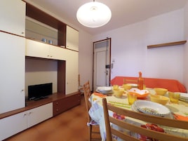 Uma área de refeições com uma mesa posta para dois, uma televisão em um suporte e um espelho sobre a mesa.