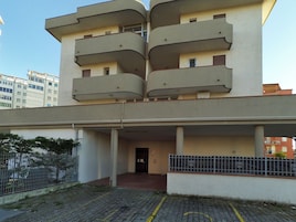 Edifício de vários andares com fachada plana, varandas e entrada protegida por portão.