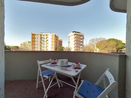 Varanda com mesa posta para dois, cadeiras e vista para prédios de apartamentos.