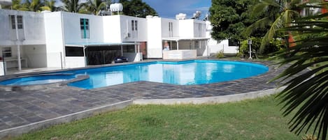 Piscina com borda curva, rodeada por um deck pavimentado e uma área gramada.