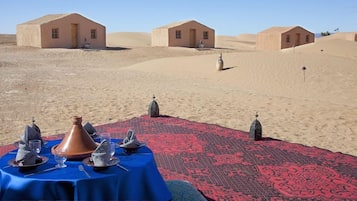 Cena de deserto com uma mesa posta para refeição, destacando uma toalha de mesa azul e um tapete vermelho com padrão.