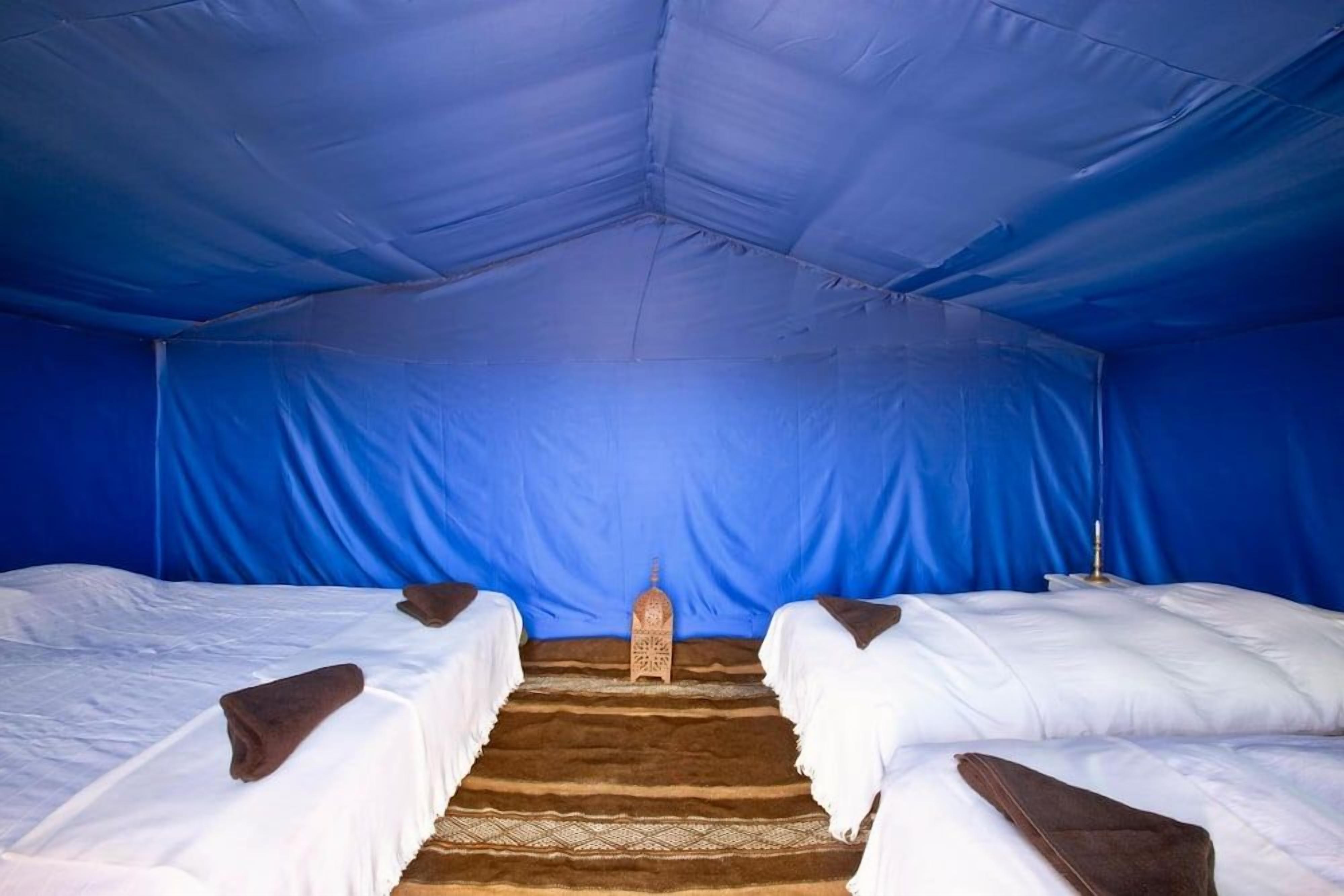 Quarto tipo tenda com duas camas, um corredor central com carpete e um candeeiro decorativo.