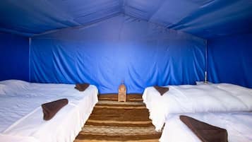 Quarto tipo tenda com duas camas, um corredor central com carpete e um candeeiro decorativo.