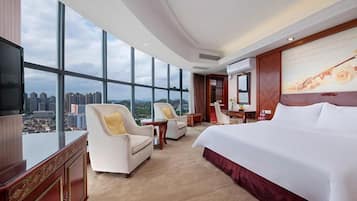 Quarto de hotel com uma cama grande, duas poltronas, uma escrivaninha e uma televisão.