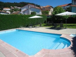 Piscina com borda azulejada, cercada por um hedge e algumas cadeiras de descanso.