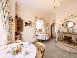 Uma sala de jantar com mesa redonda posta para quatro pessoas, lareira com objetos decorativos e um candelabro.