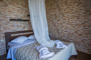 Uma cama de solteiro com cabeceira de madeira, um dossel branco pendurado e parede com padrão de tijolos.