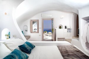 Quarto com cama, vista para o mar, banheiro com pia e espelho, e uma pequena varanda.