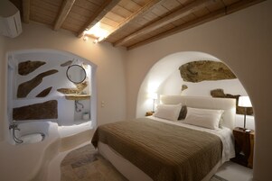 Quarto com cama grande, banheira integrada e decoração em parede de pedra.