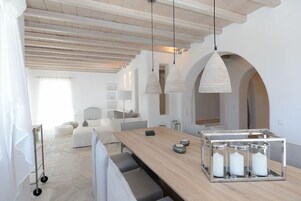 Interior moderno com mesa de jantar de madeira, assentos acolchoados e iluminação pendente.