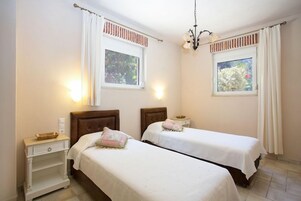 Quarto com duas camas, mesa de cabeceira, abajur e janela com cortinas.