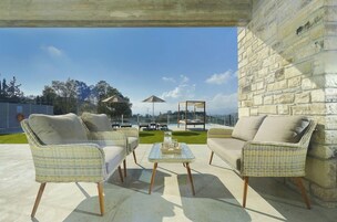 Espaço ao ar livre com móveis de vime e mesa de vidro, com vista para uma piscina e vegetação.