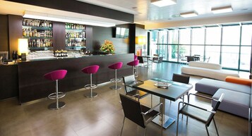 Um espaço de bar moderno com balcão, banquetes e área de estar com sofá e cadeiras.