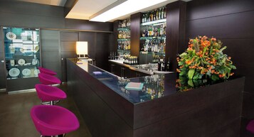 Uma área de bar com balcão de vidro, banquetas e diversos tipos de garrafas.