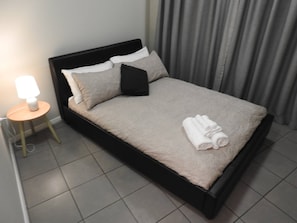 Cama bem arrumada com edredom branco, duas almofadas e uma toalha enrolada.