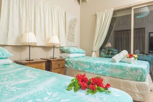 Quarto de hotel com duas camas, uma mesa de cabeceira, abajur, janela com cortinas e um adorno na parede.