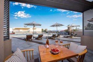 Terraço no topo com espreguiçadeiras, guarda-sóis, mesa com garrafa e copos, e um recipiente com morangos.