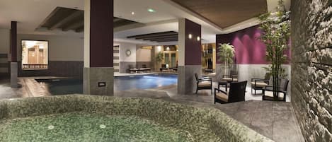 Um saguão de hotel com uma grande piscina interior, área de estar e uma parede de pedra.