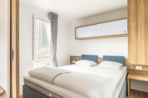 Quarto com cama, janela com cortinas, mesa de cabeceira e espelho na parede.