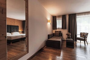 Quarto de hotel com cama, sofá, mesa pequena, cadeira e espelho.
