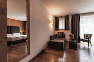 Quarto de hotel com cama, sofá, mesa pequena, cadeira e espelho.