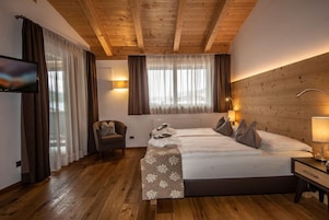 Quarto de hotel com teto de madeira, uma cama com almofadas, uma cadeira, uma televisão e uma mesa de cabeceira com abajur.