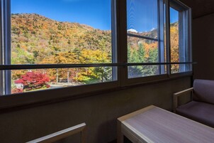 Quarto com uma grande janela que oferece vista para um morro com folhagem de outono.