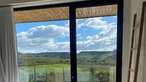 Um banheiro moderno com uma banheira separada, uma varanda envidraçada com vista para colinas verdes e uma escada de madeira.