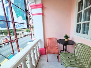 Uma varanda com vista para a rua, uma pequena mesa com uma planta e duas cadeiras.