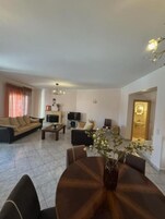 Uma sala de estar com sofá, mesa de centro, televisão e um espaço de jantar com cadeiras e mesa.