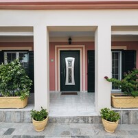 Entrada de edifício com porta central, com dois vasos de plantas de cada lado, e um pequeno degrau de acesso.