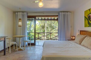 Quarto com cama, mesinha, duas cadeiras, ventilador de teto e vista para o exterior.