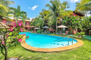 Piscina cercada por palmeiras e espreguiçadeiras.