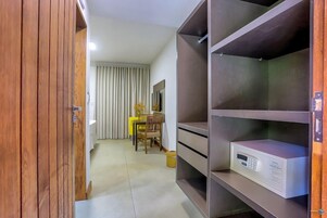 Quarto com porta de madeira, micro-ondas em prateleira, área de refeições com mesa e cadeiras, e janela com cortinas.