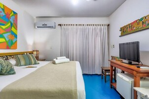 Quarto de hotel com cama, escrivaninha, televisão, ar condicionado e janela com cortinas.