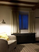 Um quarto com radiador, janela com cortinas, luminária e sofá.
