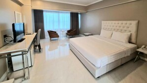 Quarto de hotel com cama, escrivaninha, cadeiras e televisão.