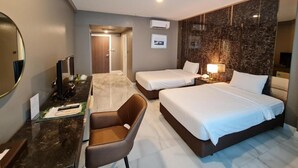 Quarto de hotel com duas camas, uma escrivaninha com cadeira, um espelho e uma televisão.