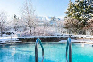 Uma piscina com água azul cristalina, rodeada por árvores cobertas de neve e um cercado branco.