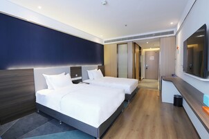 Quarto de hotel com duas camas, televisão, escrivaninha e banheiro visível por uma porta aberta.
