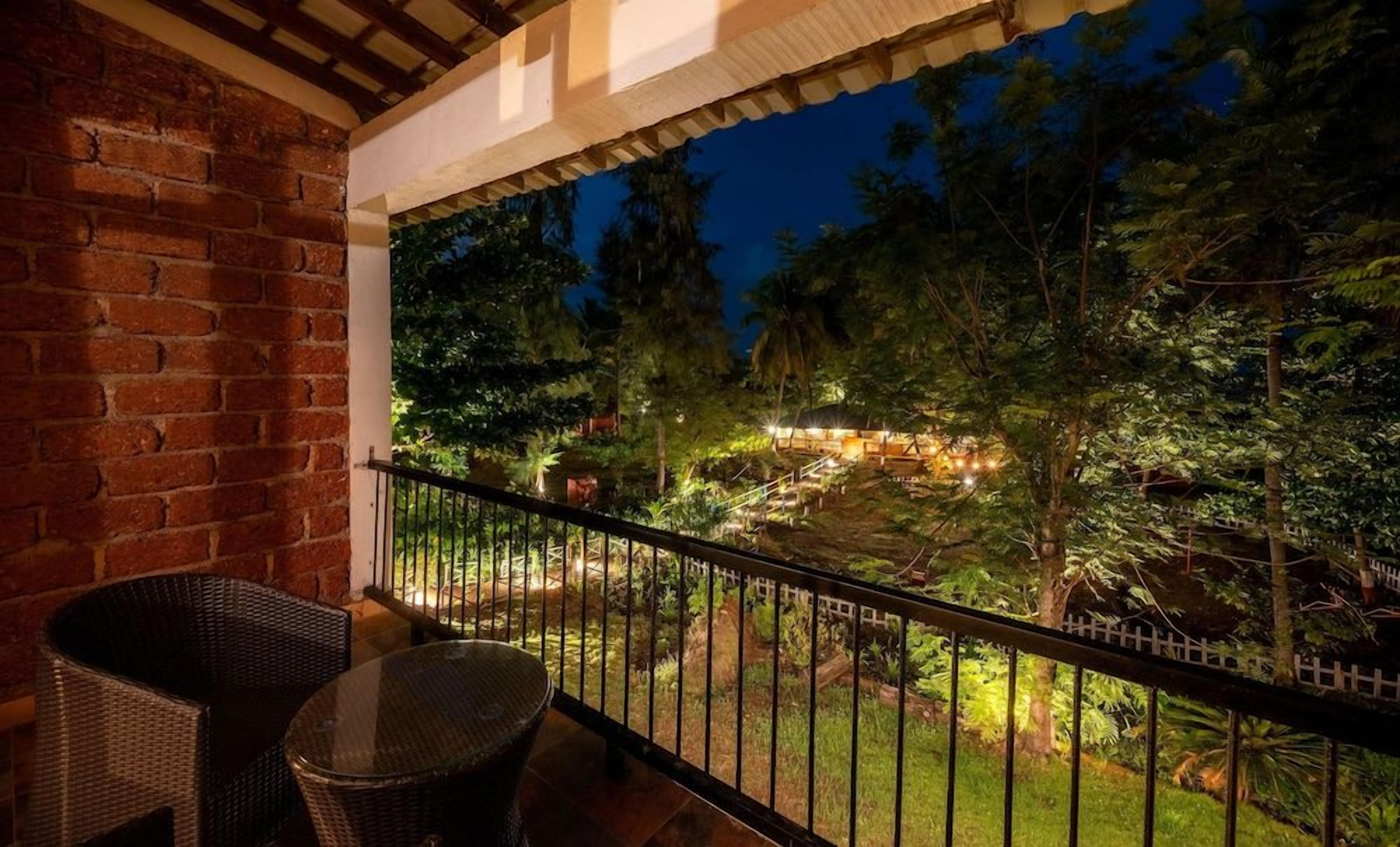 Varanda com móveis de vime, com vista para um jardim paisagístico à noite.