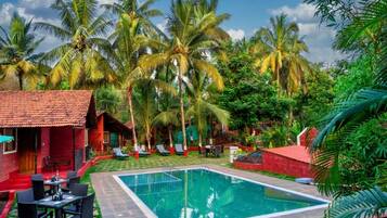 Uma área de piscina com um deck ladrilhado, cadeiras de descanso e um prédio com telhado vermelho.