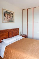 Quarto com cama de madeira, mesa de cabeceira, guarda-roupa e um quadro na parede.