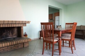 Uma sala de jantar com lareira de tijolos, cadeiras de madeira e piso de azulejos.