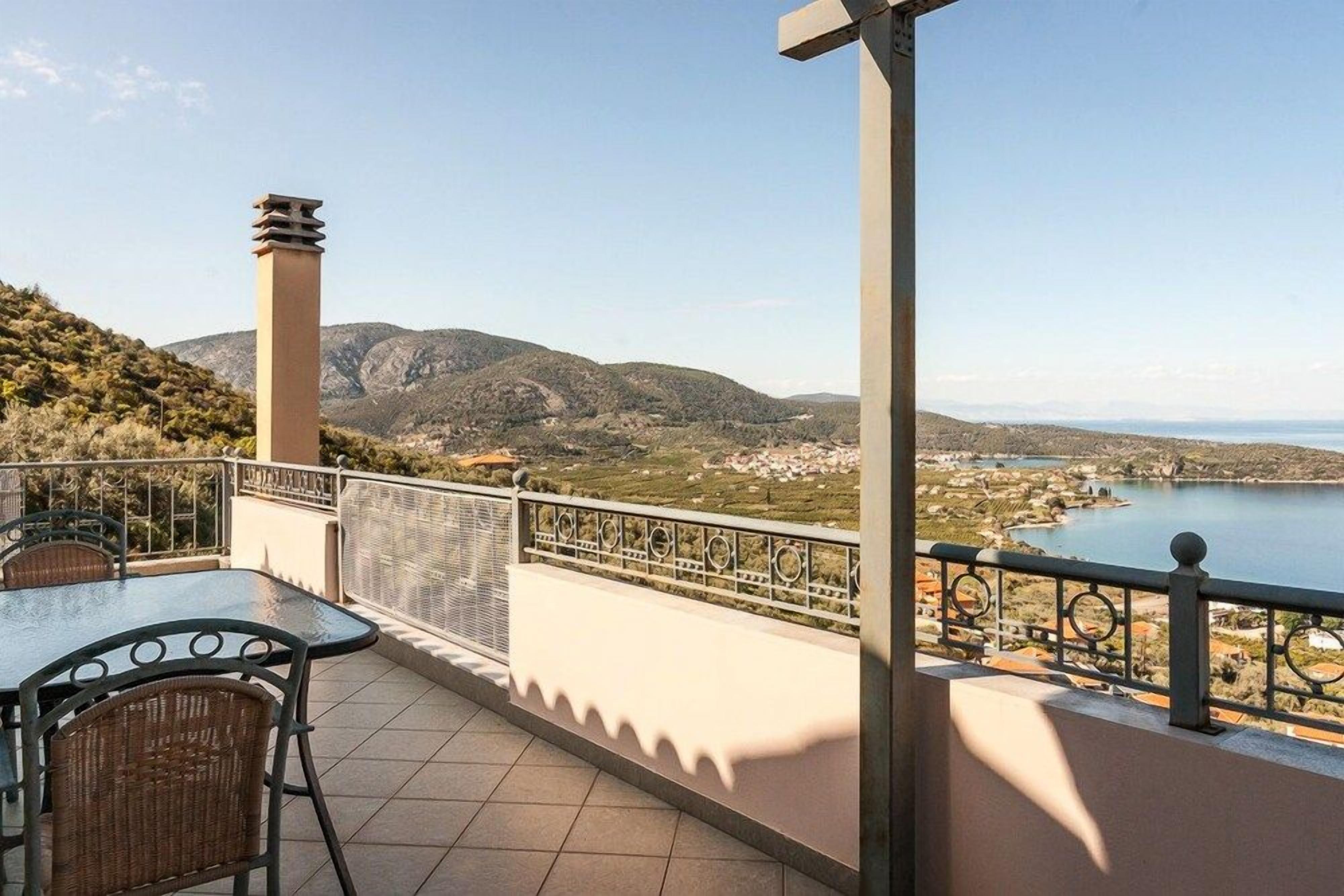 Varanda com mesa e cadeiras, vista para um corpo d'água e colinas ao longe.