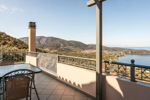 Varanda com mesa e cadeiras, vista para um corpo d'água e colinas ao longe.